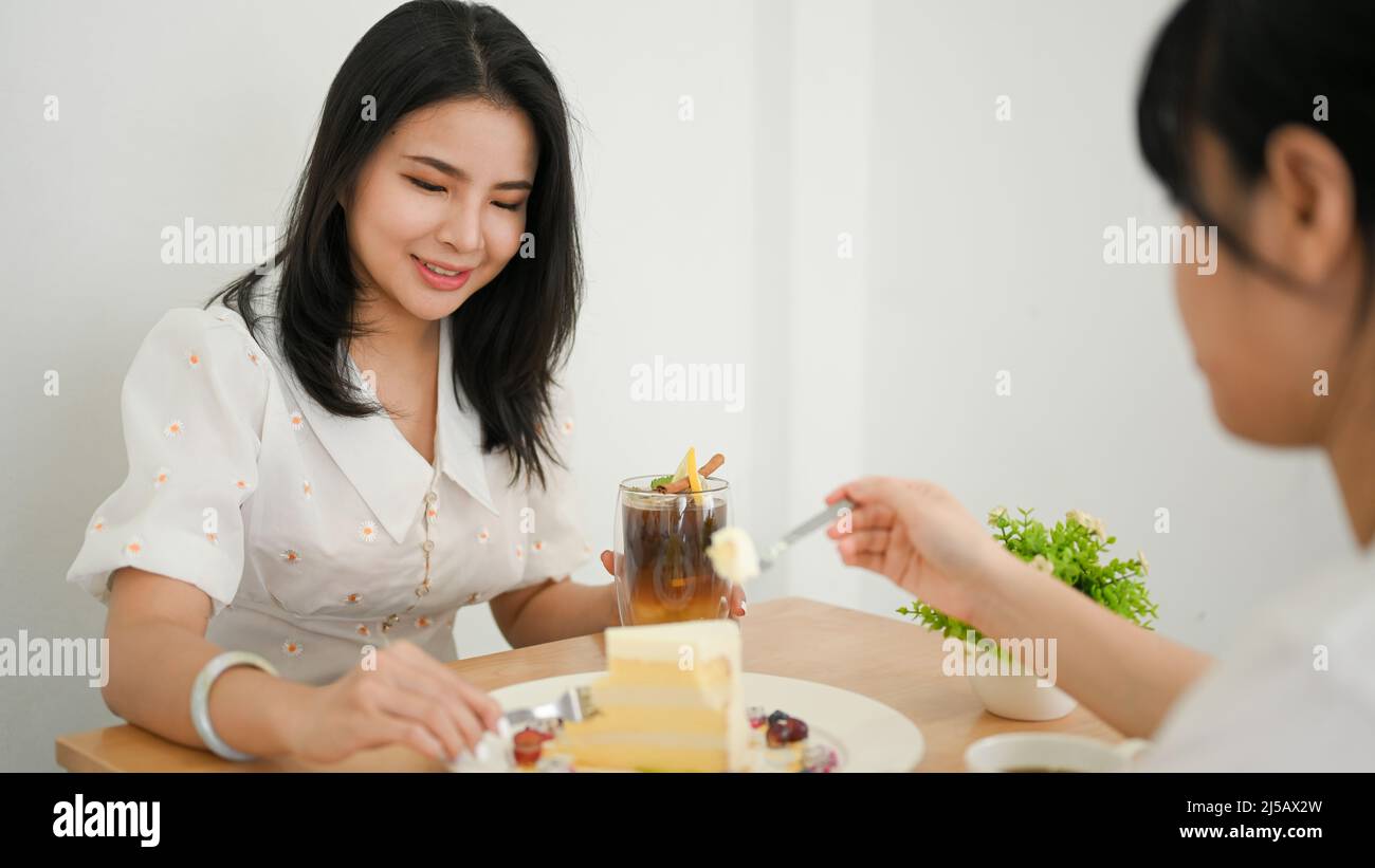 Two beautiful Asian young women enjoy talking and eating cake in the ...