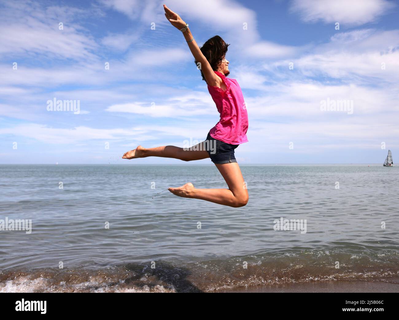 slender girl performs a high jump on the seashore in jeans fabric short ...