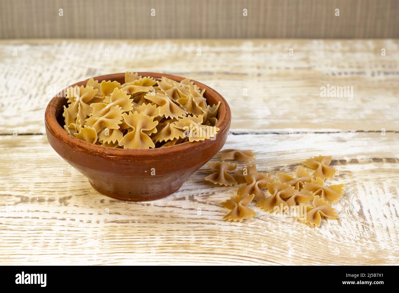 Whole grain dark pasta bows on brown plate on a rough wooden light ...