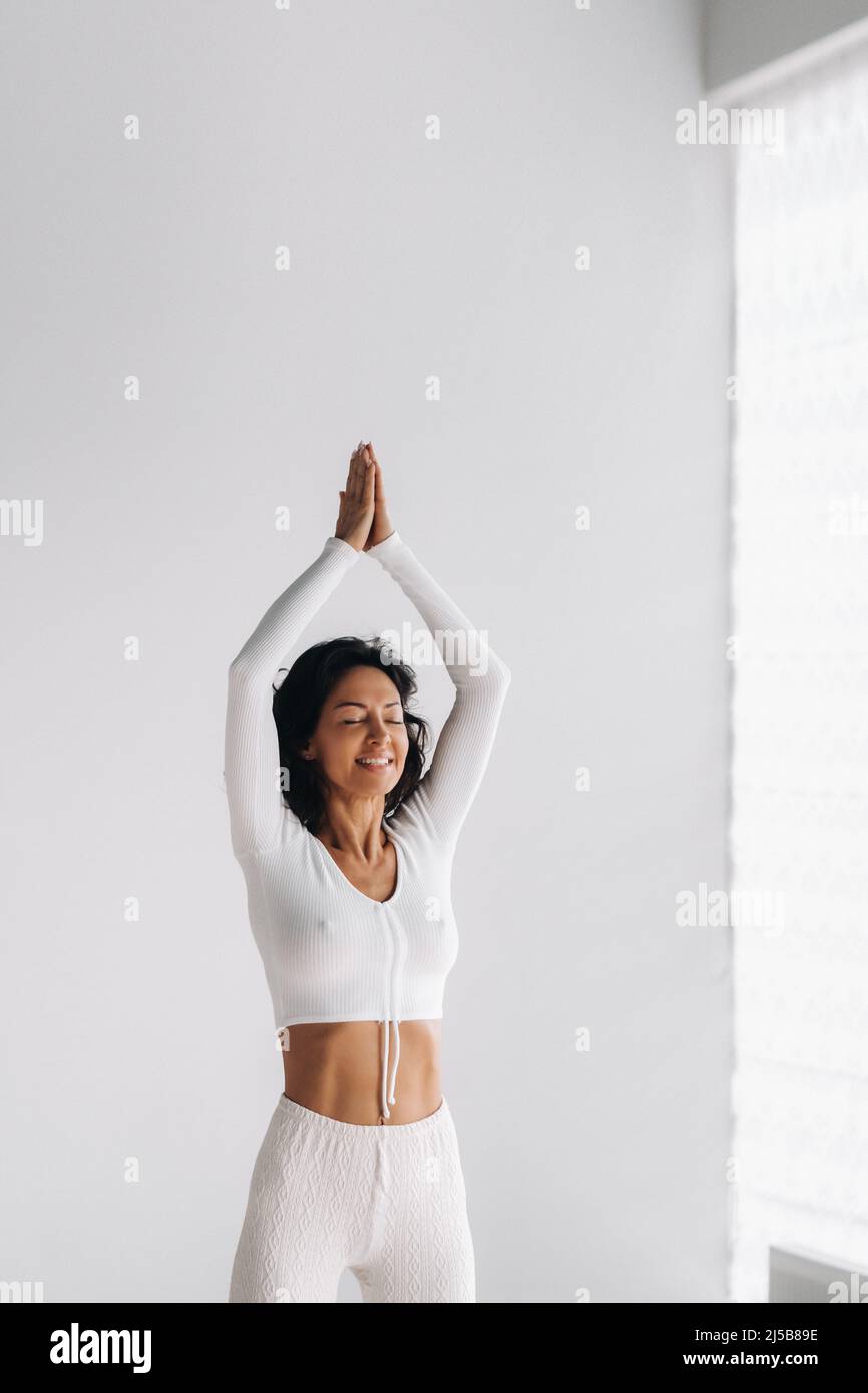a female yogi in white clothes with her hands up meditates in the Yoga ...
