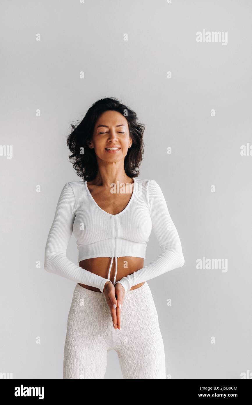 a female yogi in white clothes stands with her hands clasped at the ...
