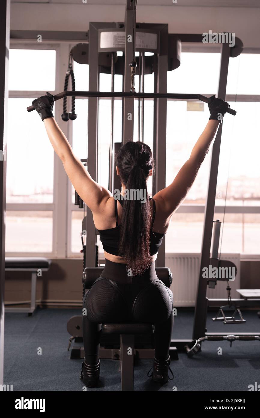 Rear view of a young fitness lady in black sportswear sitting on a gym ...