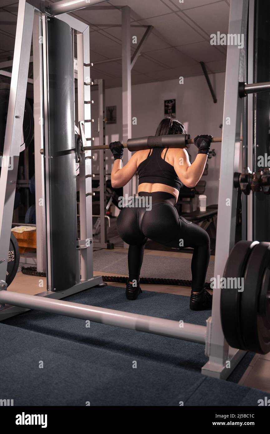 rear view of fit beautiful girl doing barbell squat in gym. Development ...