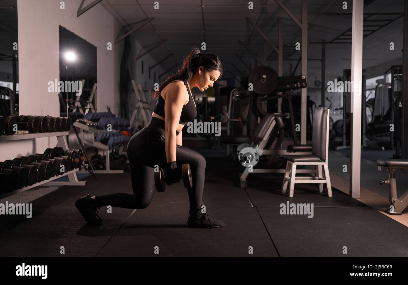 Fitness woman doing lunge exercises with dumbbells in her hands to ...