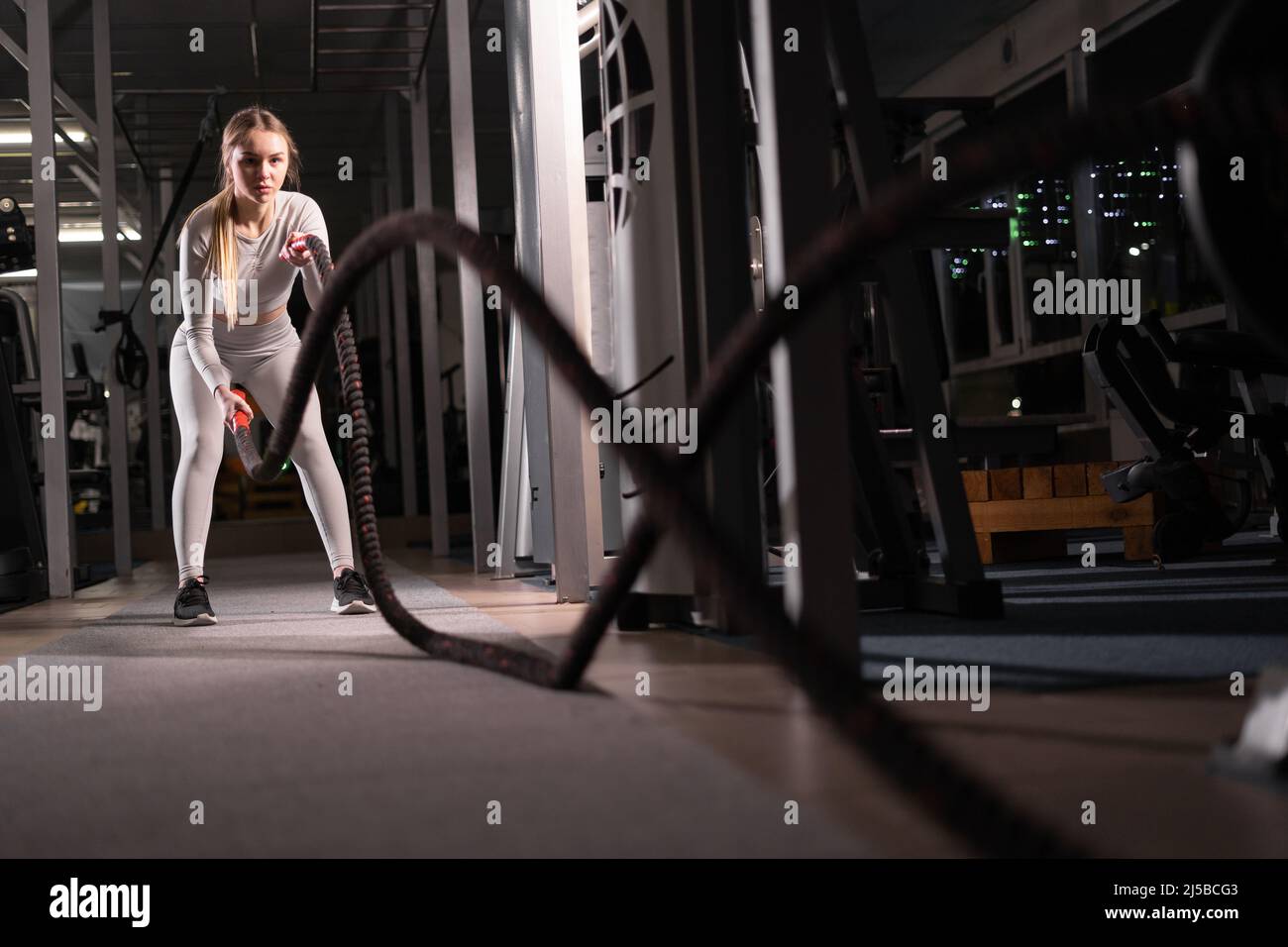 Active motivated sportswoman trains in the gym with battle ropes ...