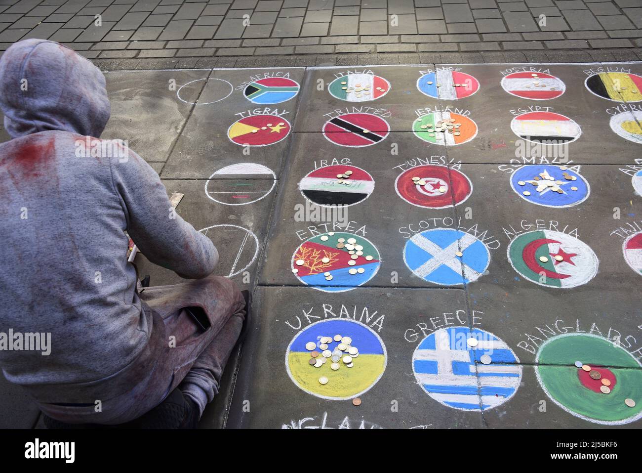 A pavement artist, wearing a grey tracksuit, draws images of many ...