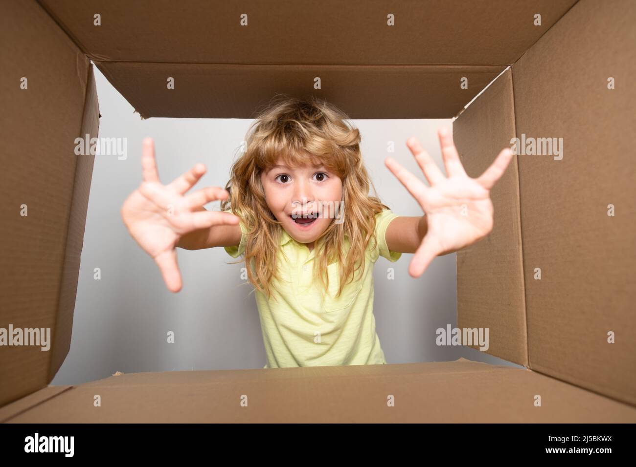 Child opens carton box and pulling out gift from it. Small boy looking ...