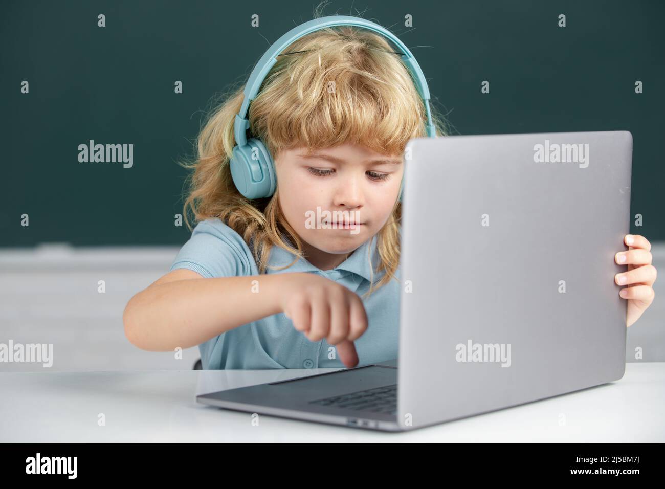 Cute boy wearing headphones, study with laptop in classroom, listening ...