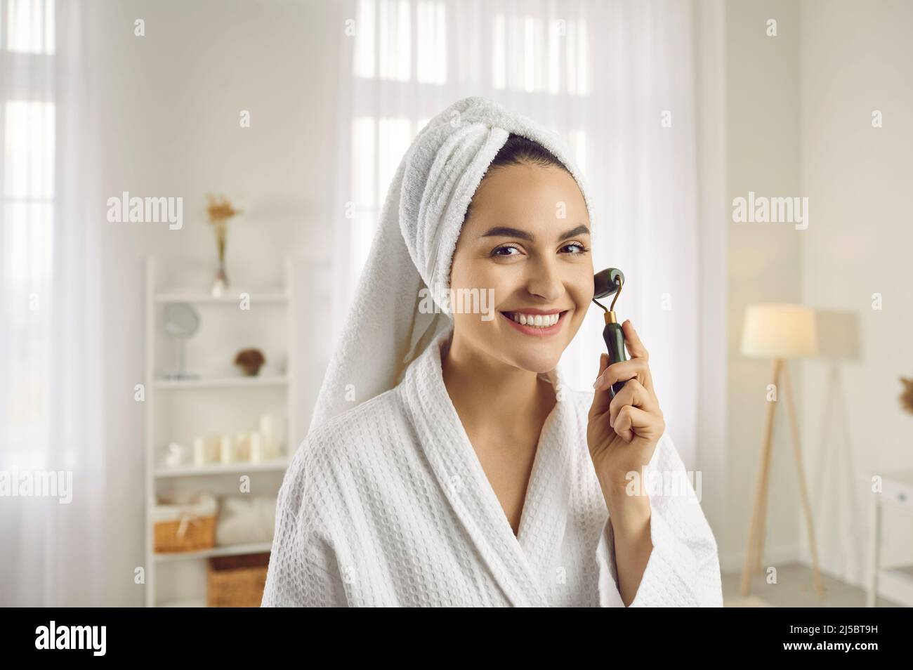 Beautiful woman massaging face with facial roller to increase blood ...