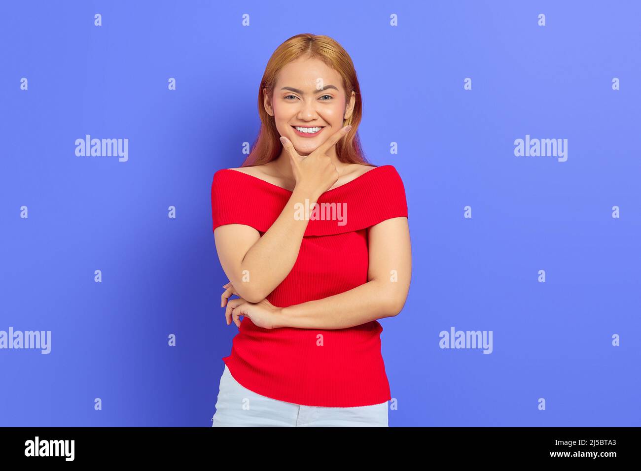Portrait of cheerful Asian woman in red dress thinking and touching ...