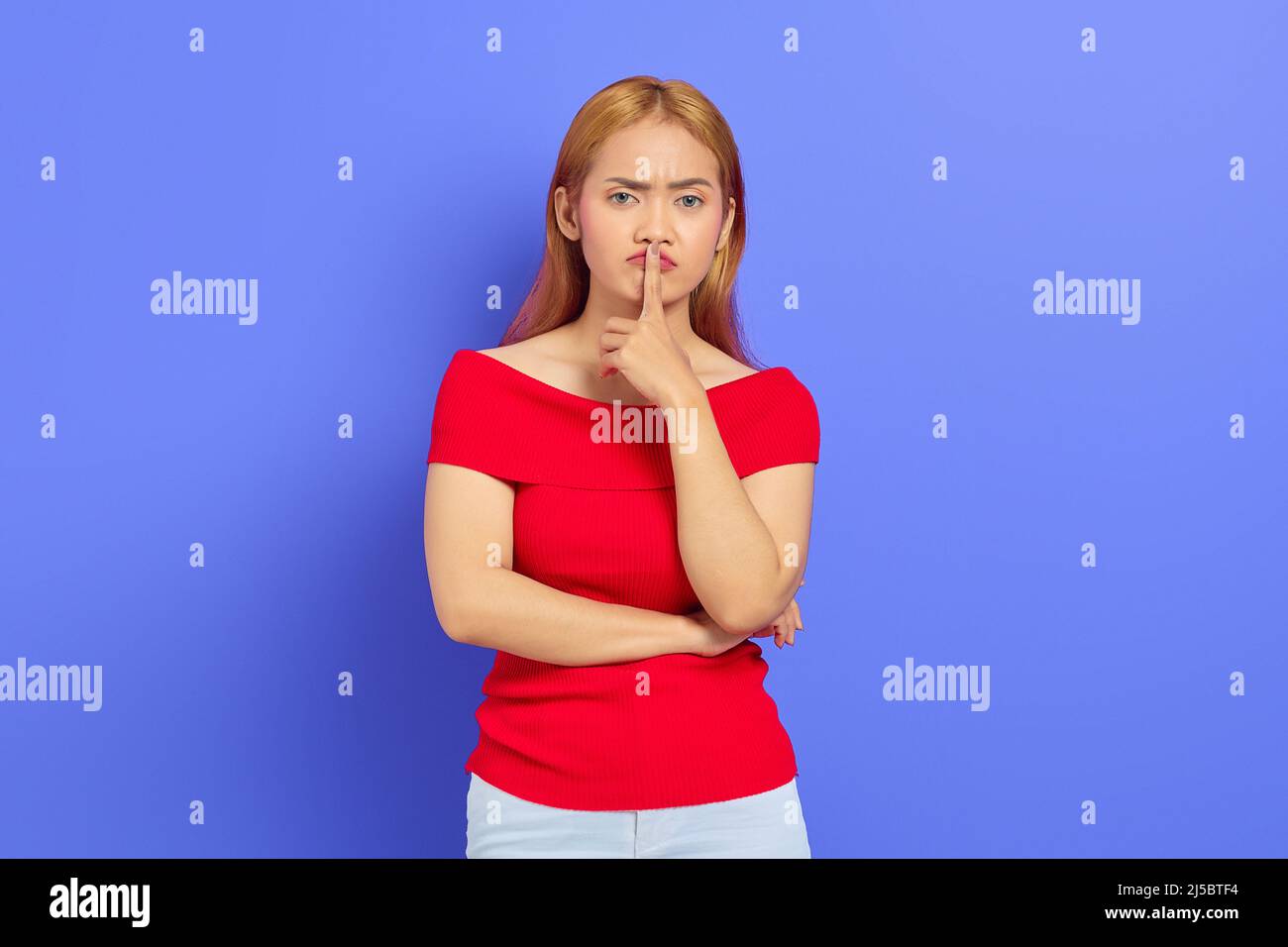 Portrait of serious Asian woman in red dress frowning and holding ...