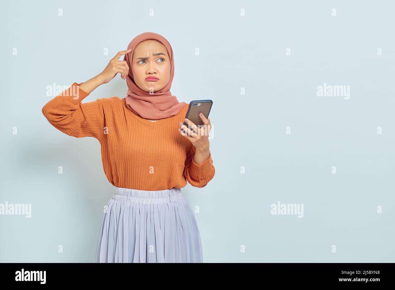 Portrait of confused young Asian Muslim woman in brown sweater hijab ...