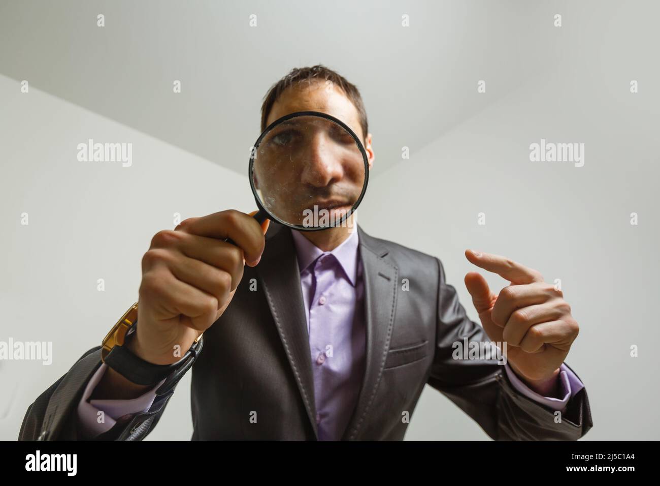 young male detective holding magnifying glass by right eye while ...
