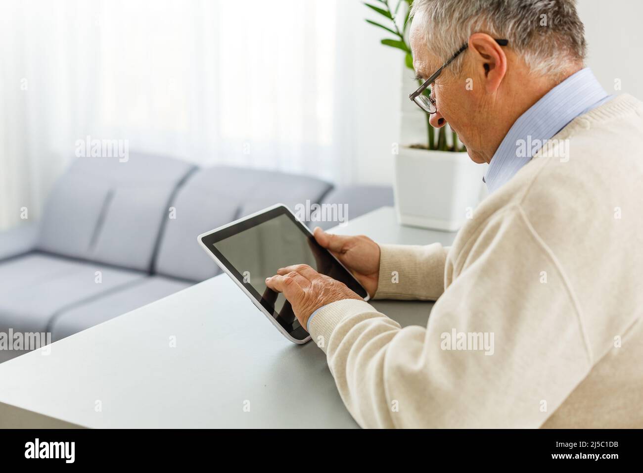 Handsome cheerful senior man using digital tablet sitting at the table ...