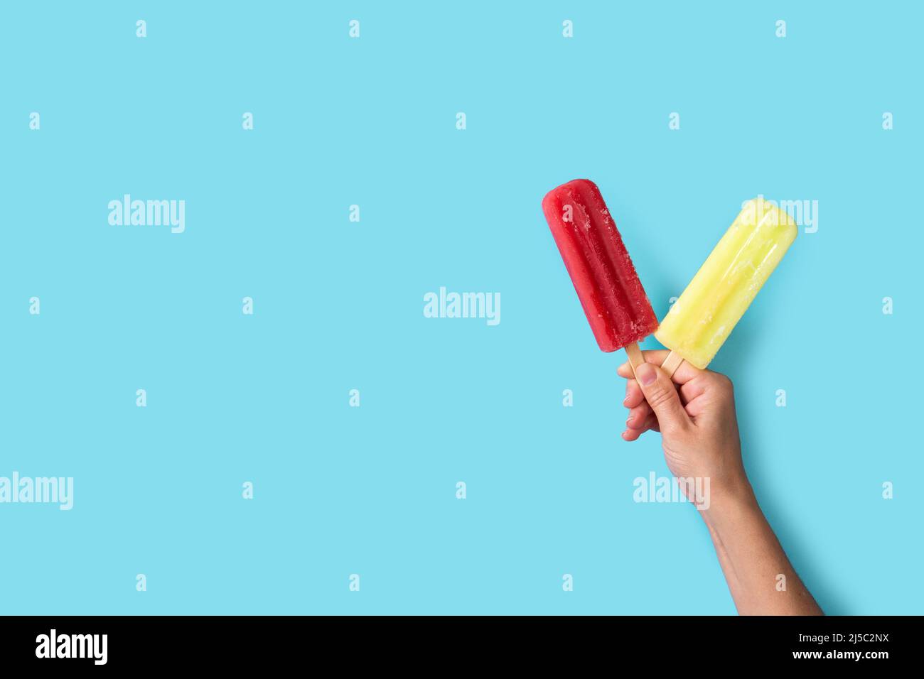 Hand holding a strawberry and lemon popsicles on blue background Stock ...