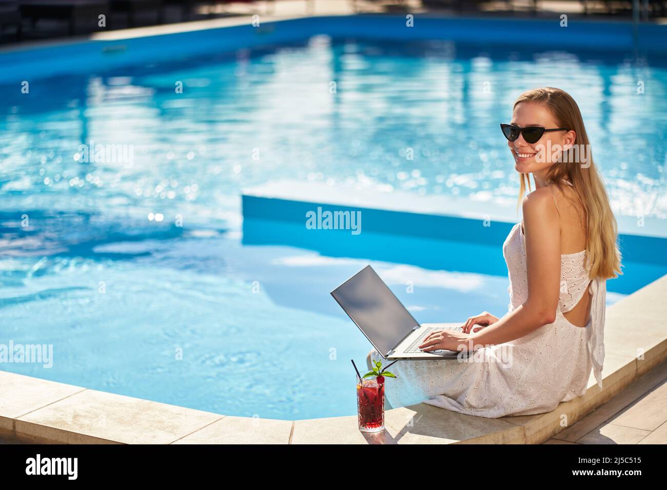 Self employed woman doing remote work with laptop sitting near swimming ...