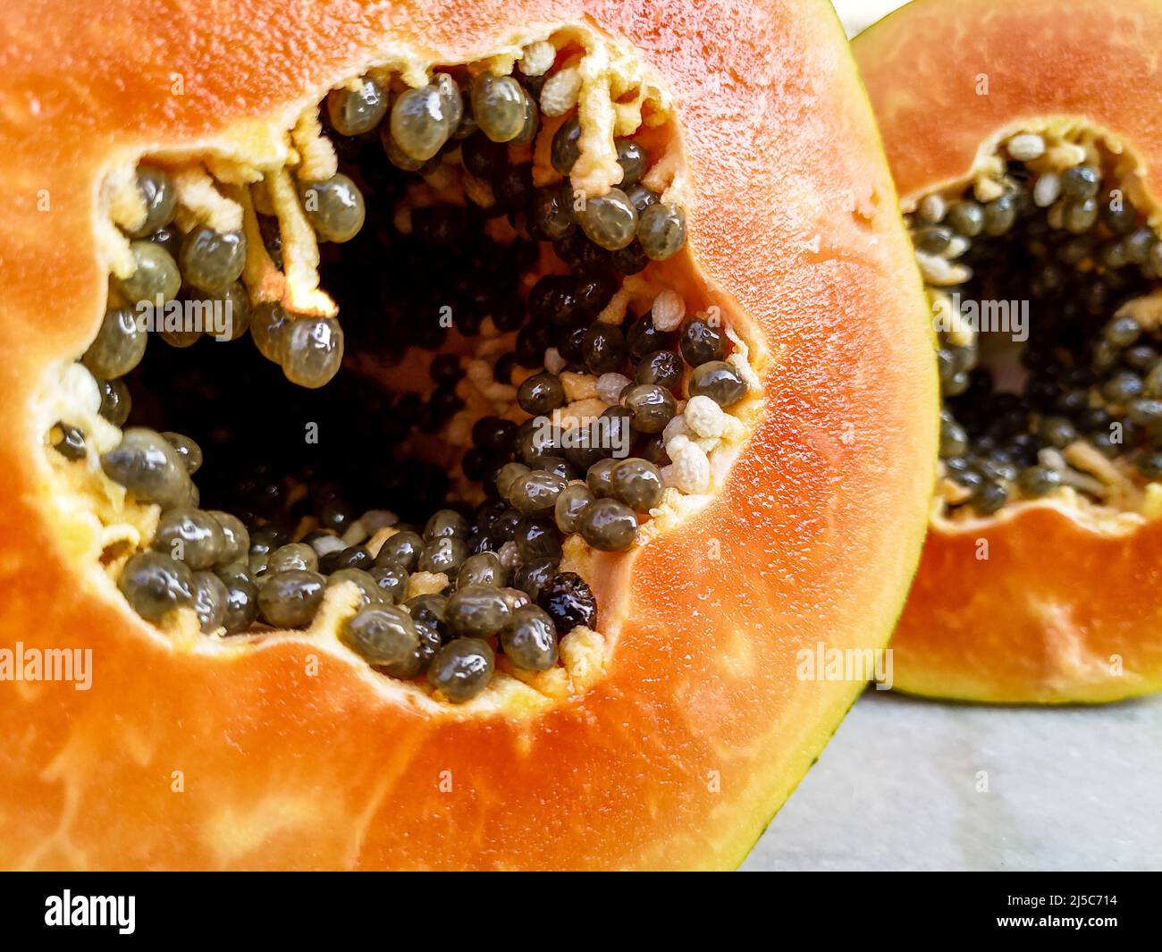 A closeup up shot of a juicy papaya fruit cut in half full of seeds ...