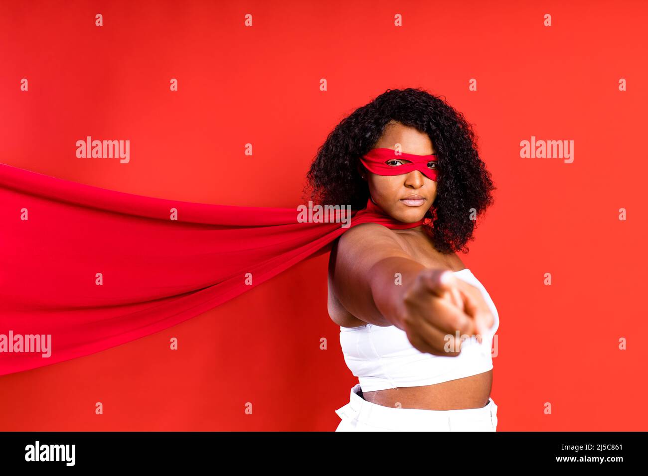 latin hispanic woman in red eye mask and long superhero cloak in studio ...