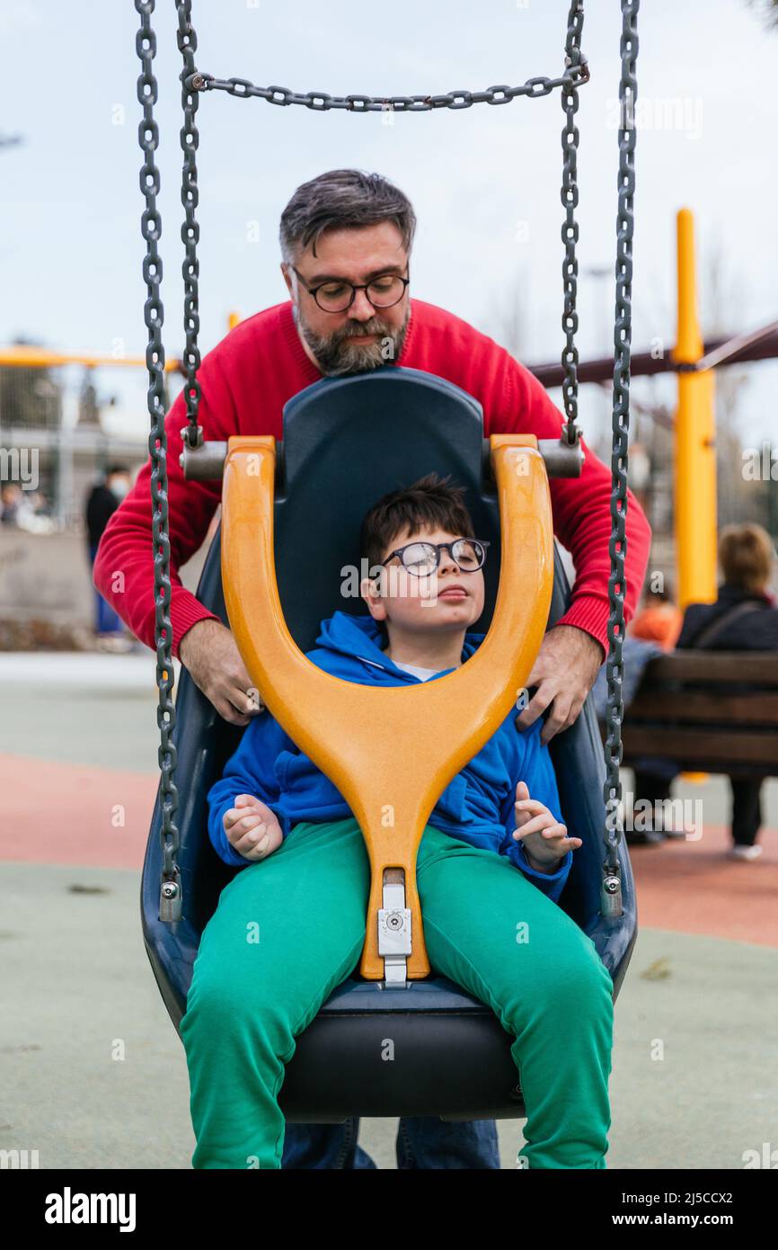 A relaxed child with a disability playing on adapted swing with his dad ...
