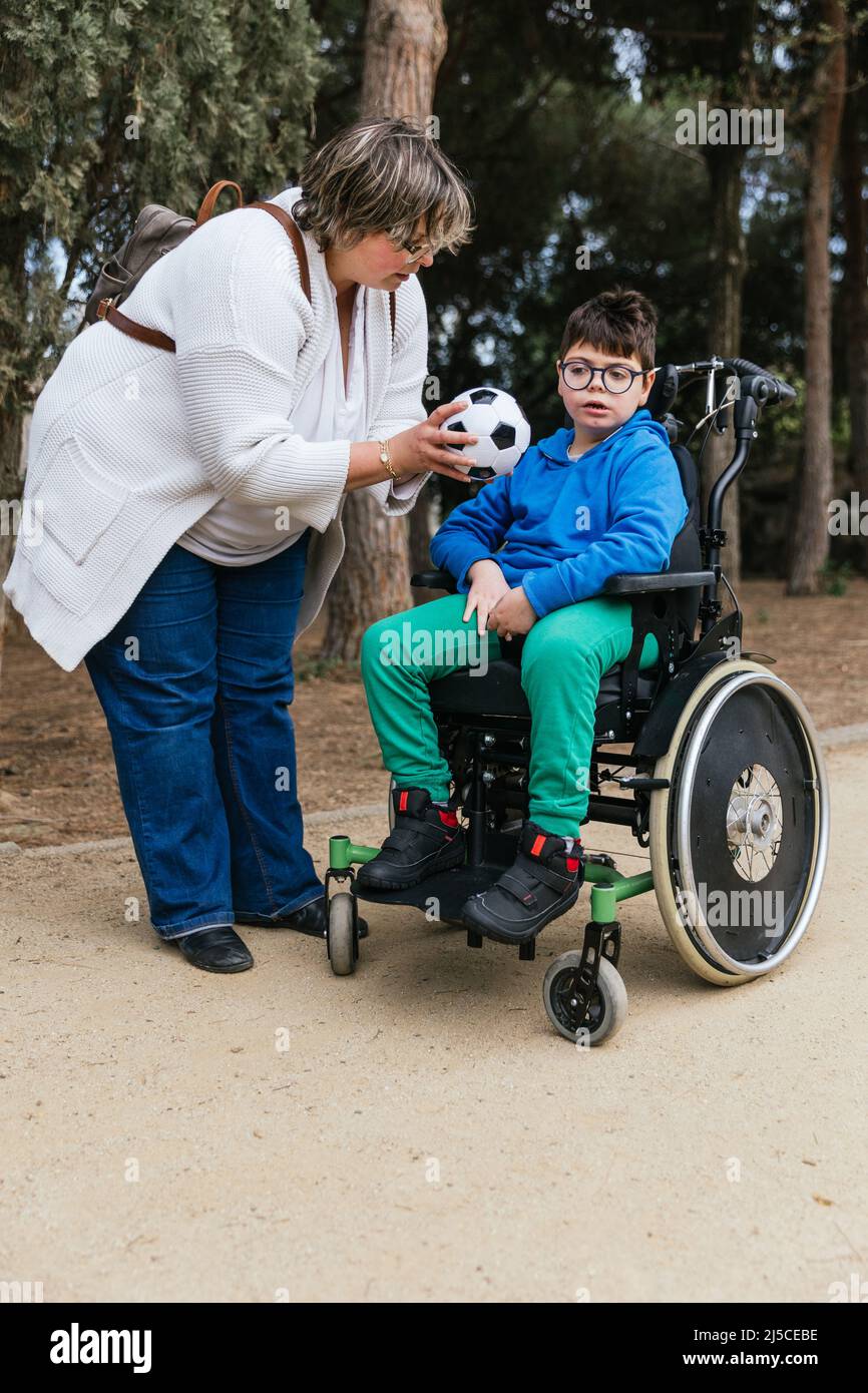A mother giving a soccer ball to her son with a disability who uses a ...