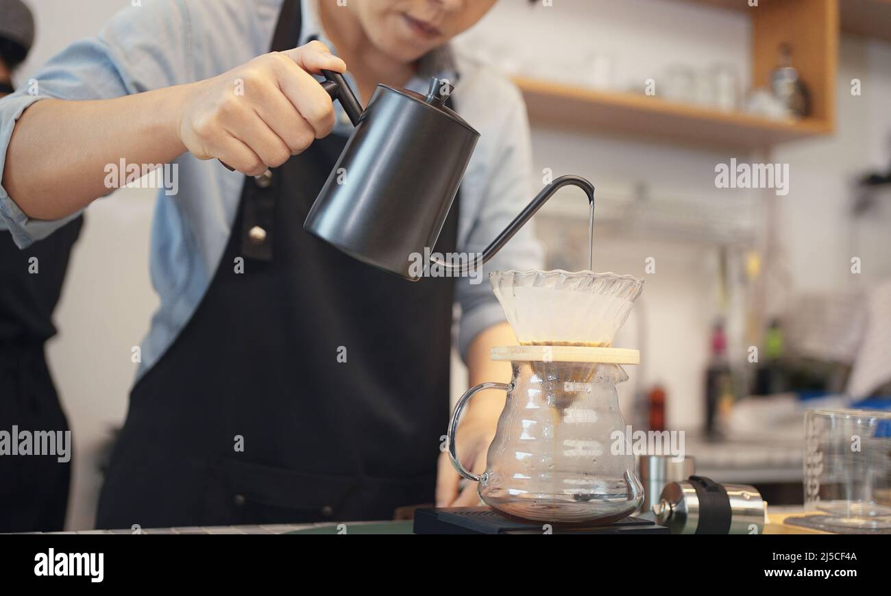 A female cafe operator wearing an apron pours hot water over roasted ...