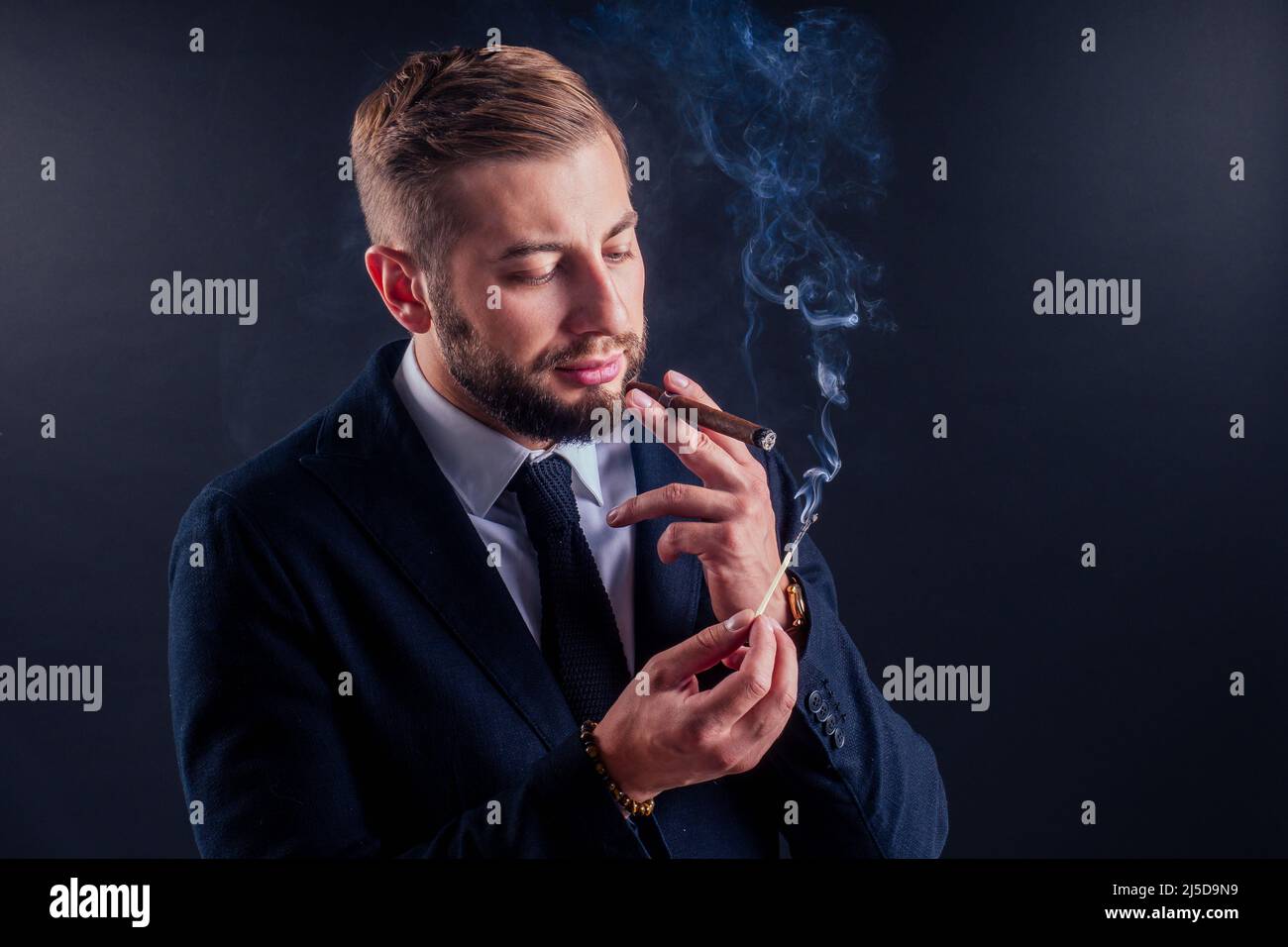 Portrait of an attractive business man with a cigar in black background ...