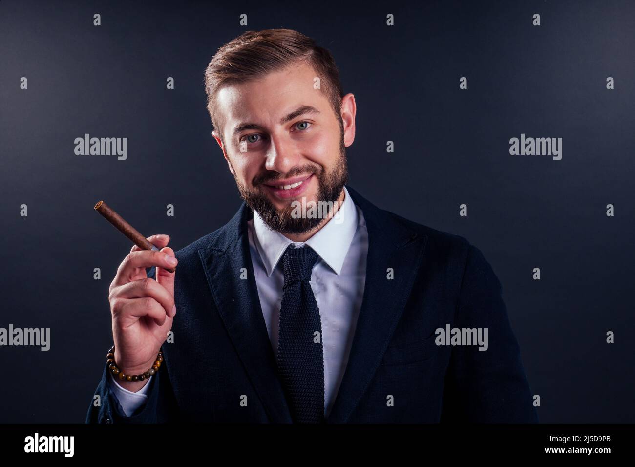 Portrait of an attractive business man with a cigar in black background ...