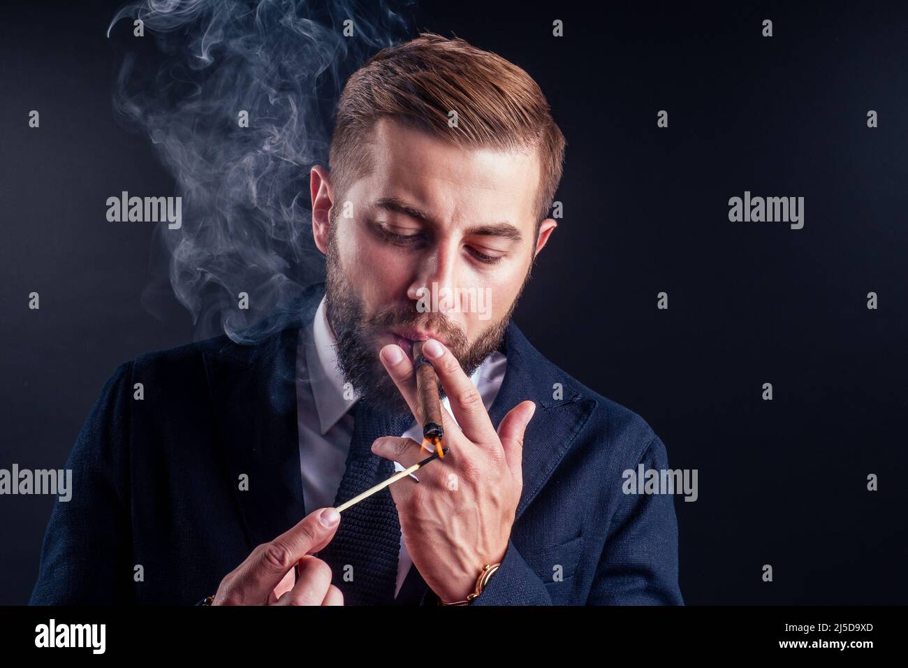 Portrait of an attractive business man with a cigar in black background ...