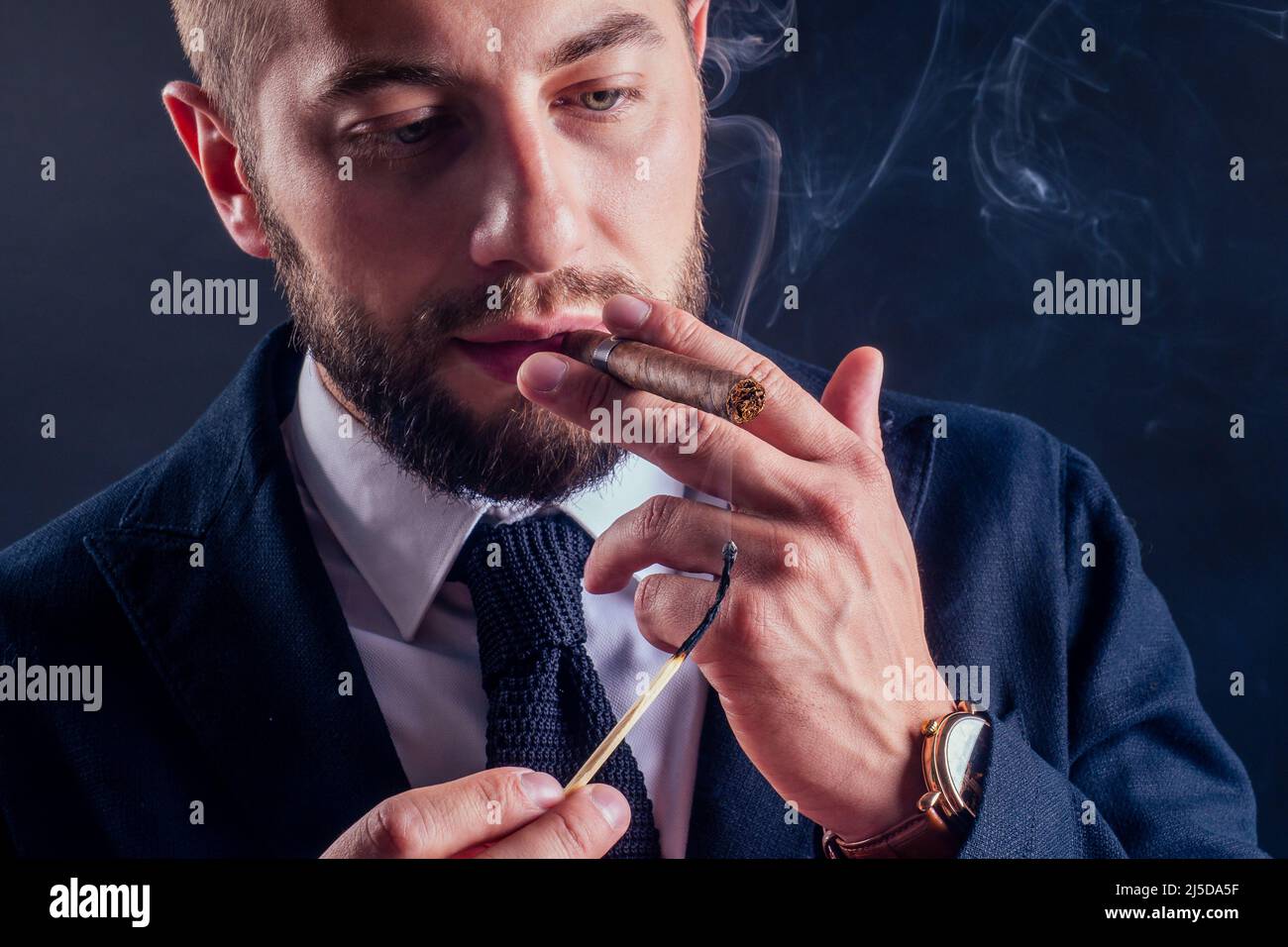 Portrait of an attractive business man with a cigar in black background ...