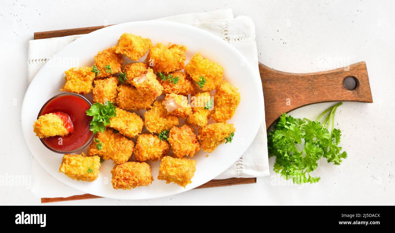 Crispy fried breaded chicken bites on white plate over light stone ...