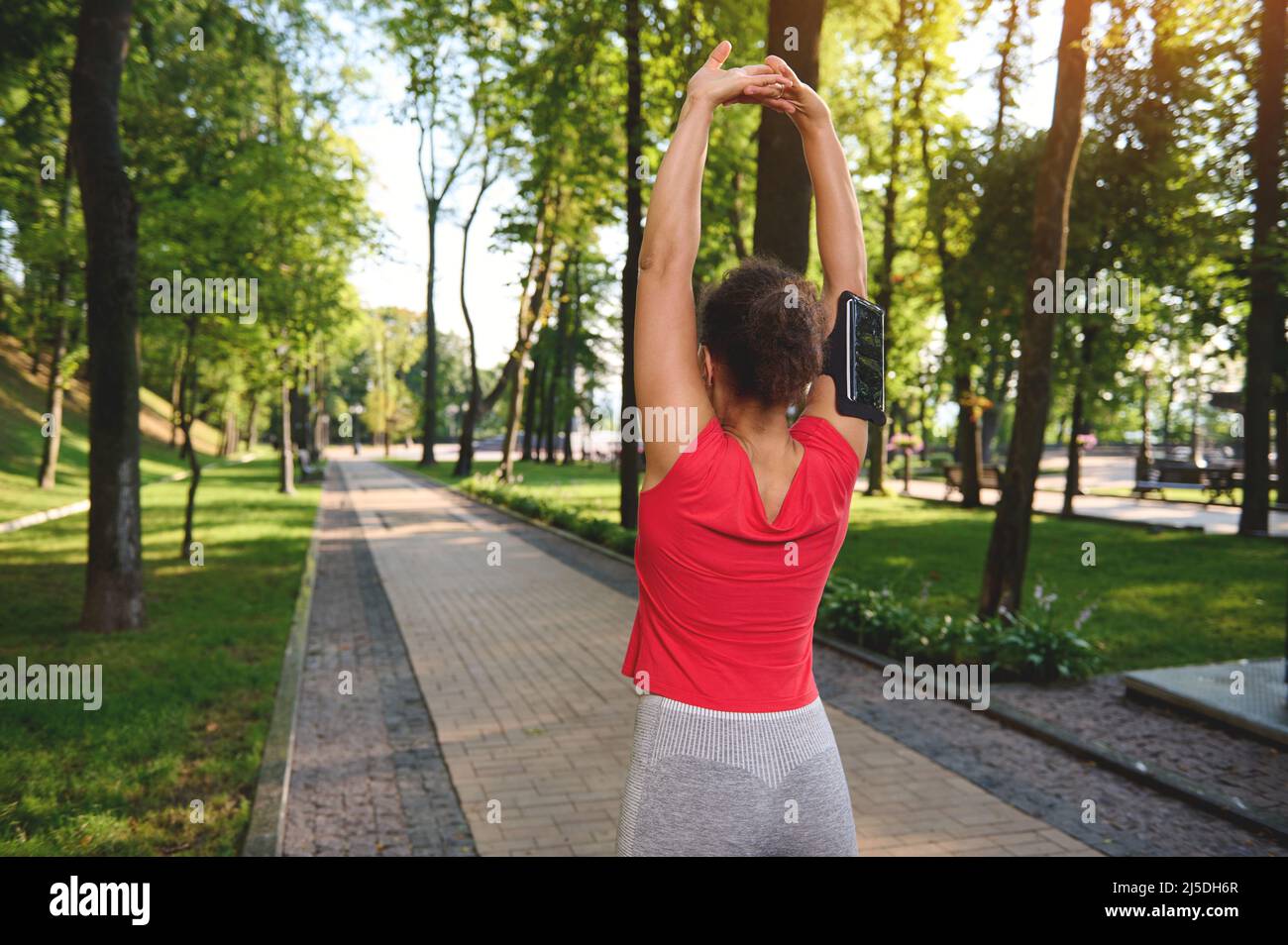 View from the back to a muscular fit athlete, sportswoman raising arms ...