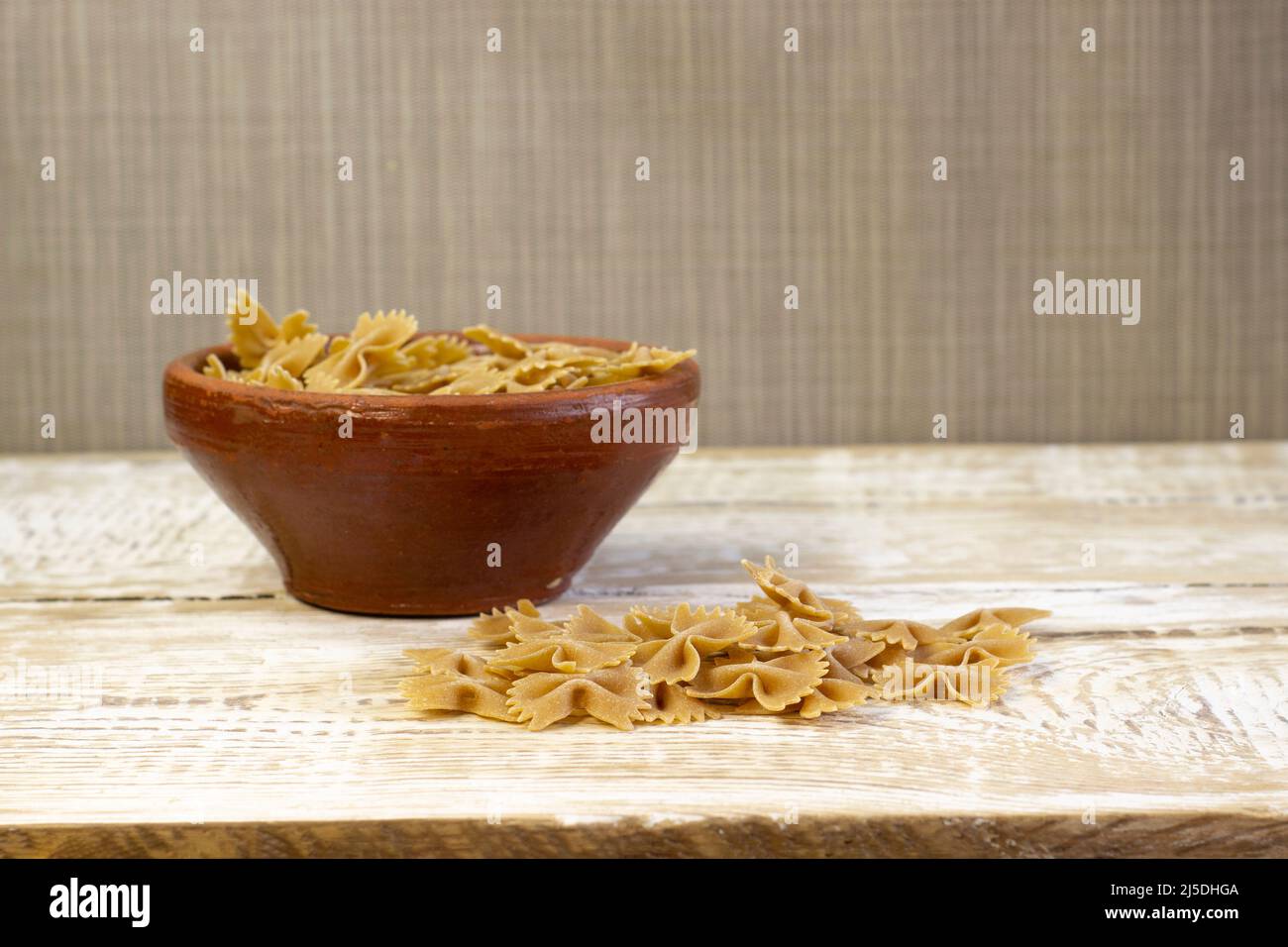 Whole grain dark pasta bows on brown plate on a rough wooden light ...