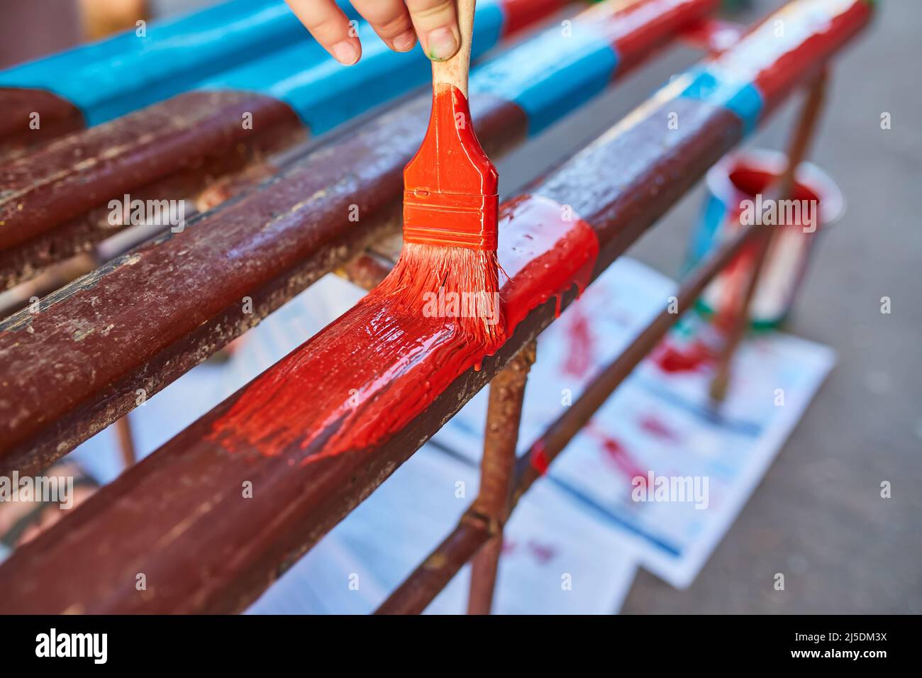 brush in hand paints a bench in bright colors, painting a garden bench ...