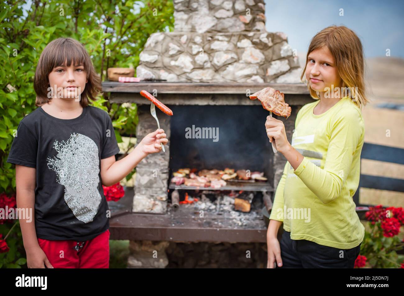 Children grilling meat. Boy and girl making barbecue on the grill on ...