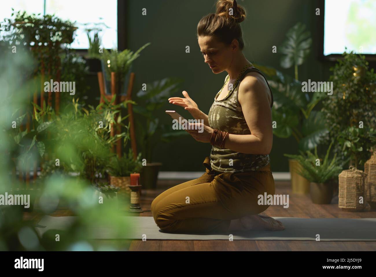 sad modern woman with smartphone doing yoga at modern green home Stock ...
