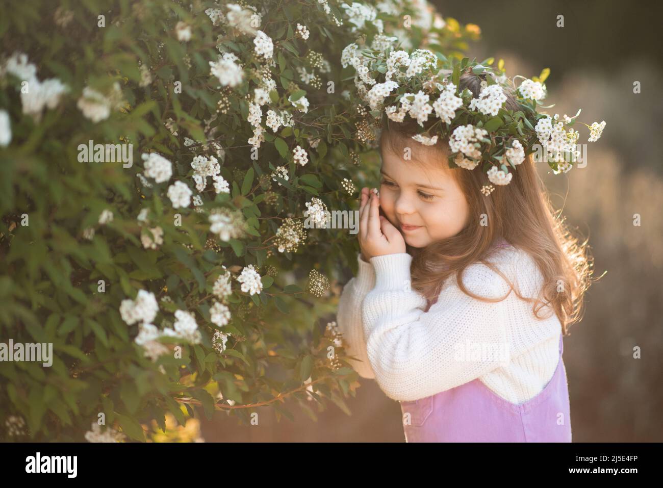 Cute child girl 3 - 4 year old wear floral wreath smelling white flower ...