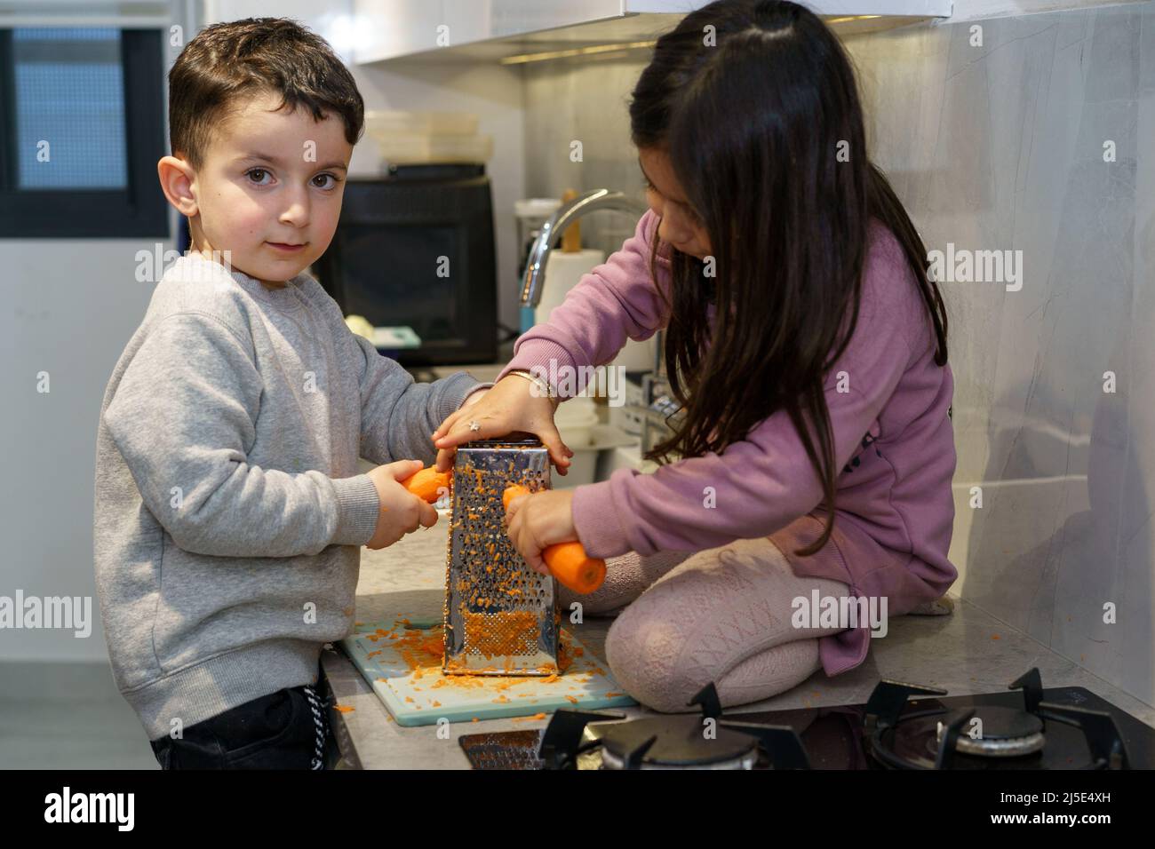 Brother and sister cook in the kitchen together, grating carrots ...