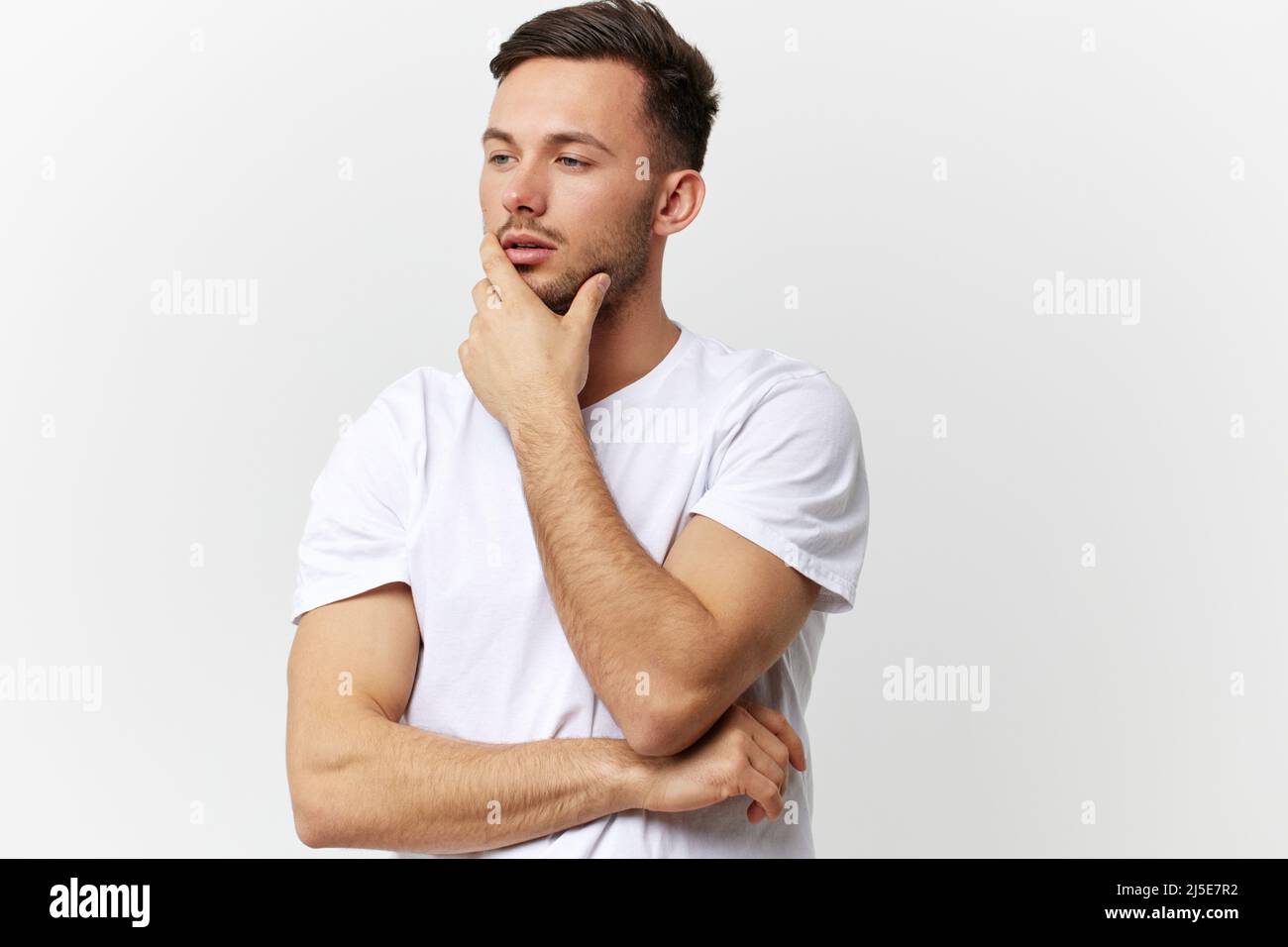 Pensive thoughtful sad tanned handsome man in basic t-shirt touch chin ...