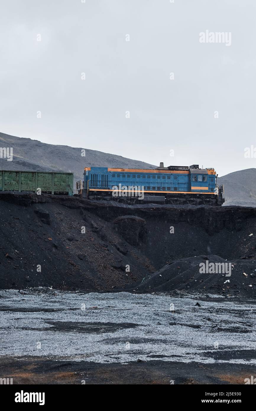 Freight train crossing polluted area with black sand hills as result of ...