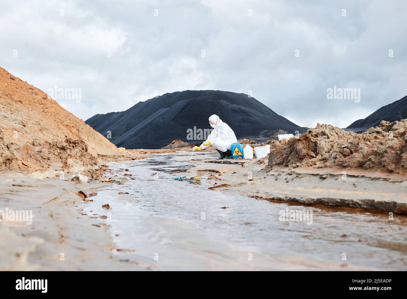 Ecologist in white hazmat suit sitting at river and using pipette while ...