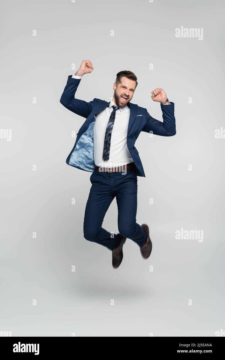 excited businessman showing triumph gesture while levitating on grey ...