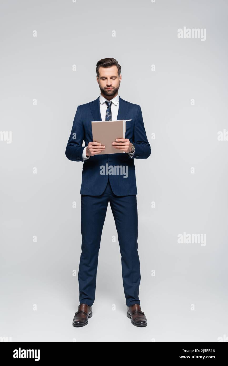 full length view of businessman in blue suit holding folder on grey ...