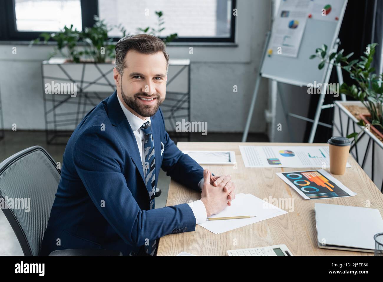 happy economist looking at camera while sitting at workplace in office ...