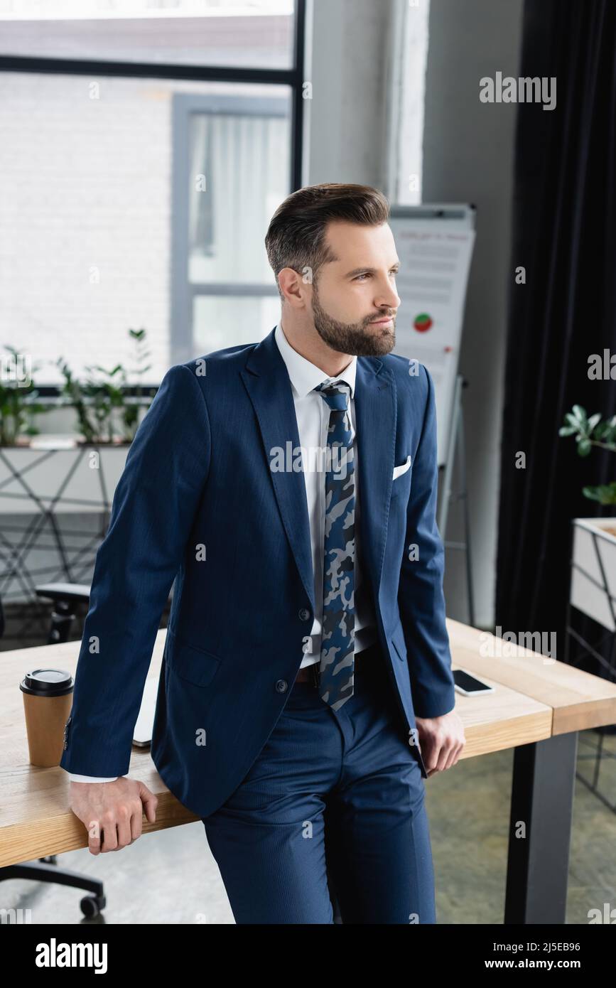 economist in suit standing at workplace in office and looking away ...