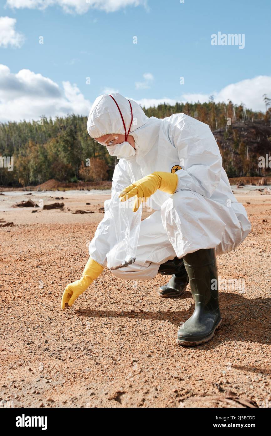 Ecologist in hazmat suit crouching on land and collecting samples of ...