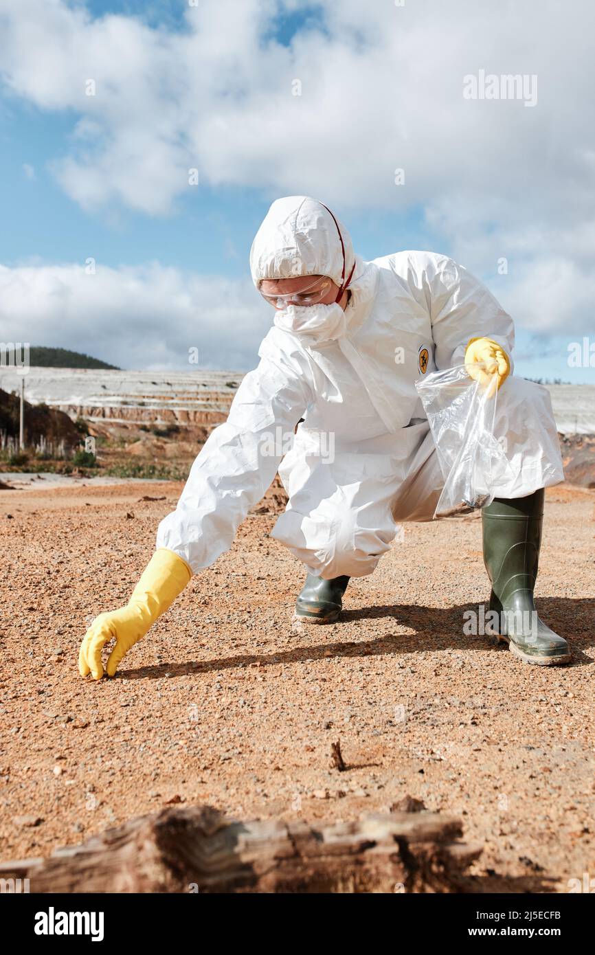 Environmental researcher in mask and safety goggles taking sample of ...