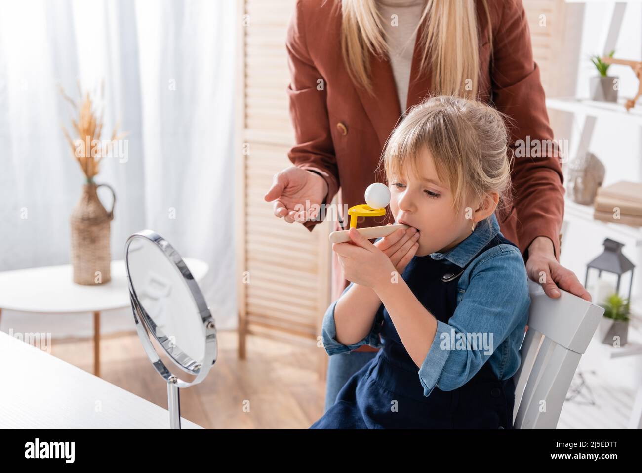 Girl using respiratory muscle trainer near mirror and speech therapist ...