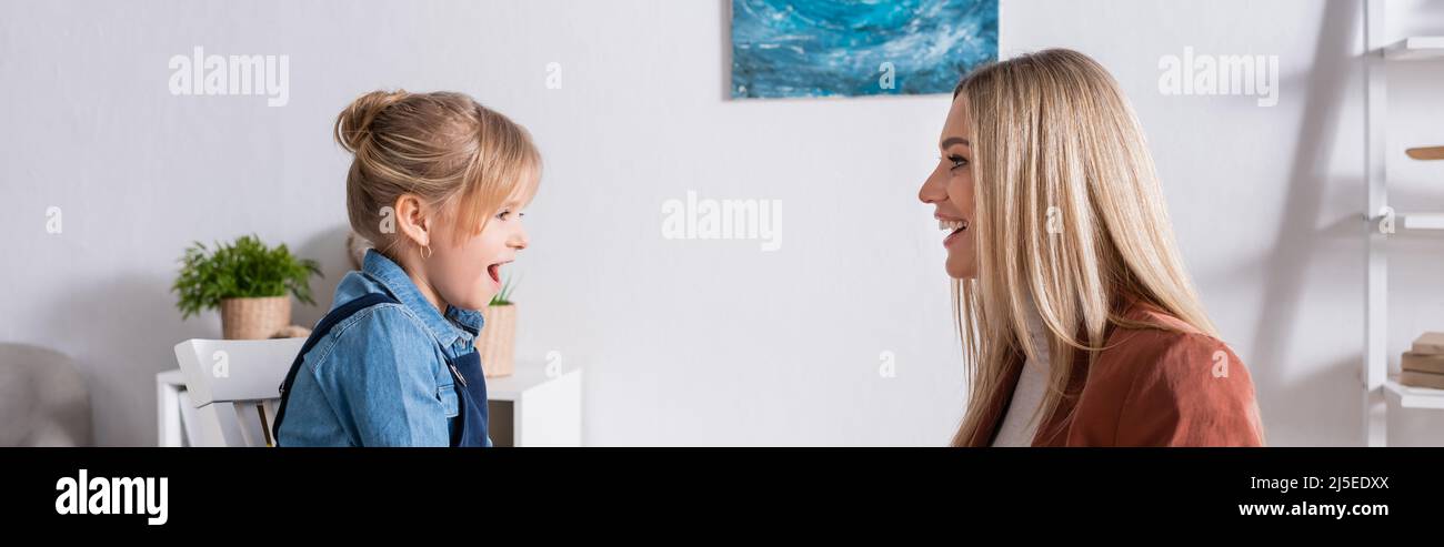 Side view of child talking near smiling speech therapist in consulting ...