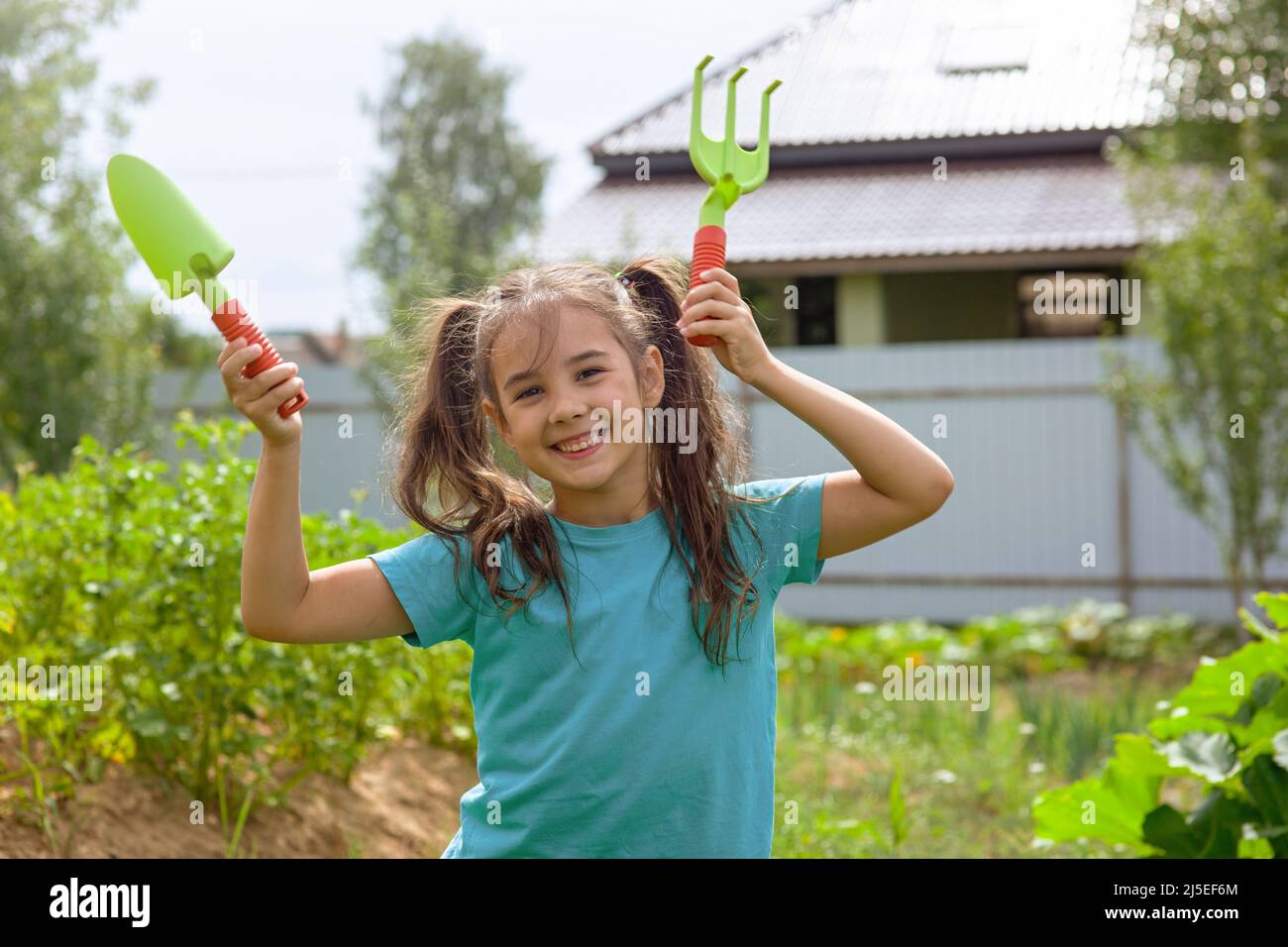 Cute little girl holding small gardening tools , dancing in the garden ...