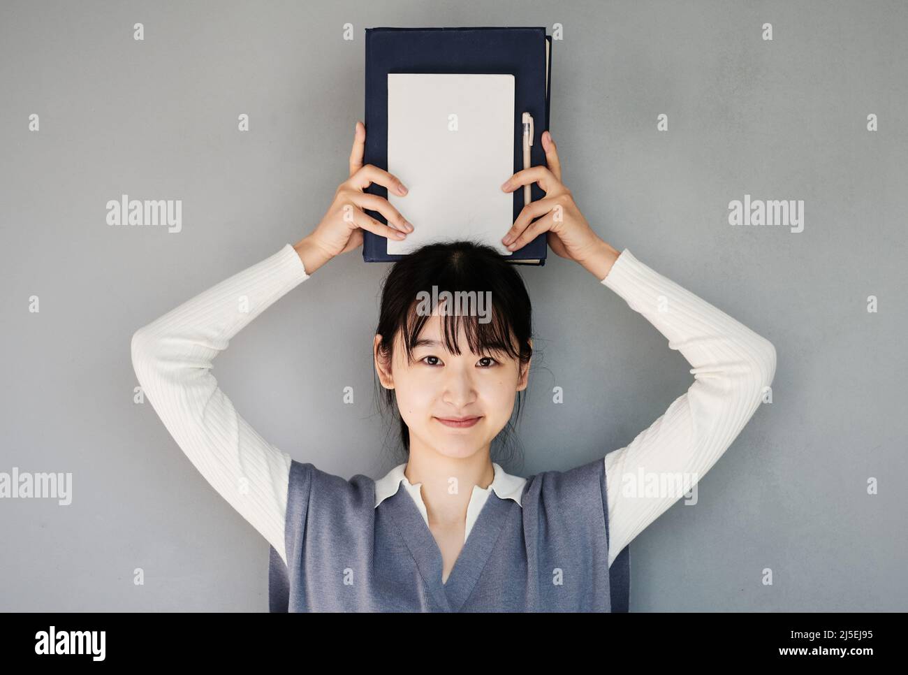 Portrait of content Asian student girl with bangs holding textbook, pen ...